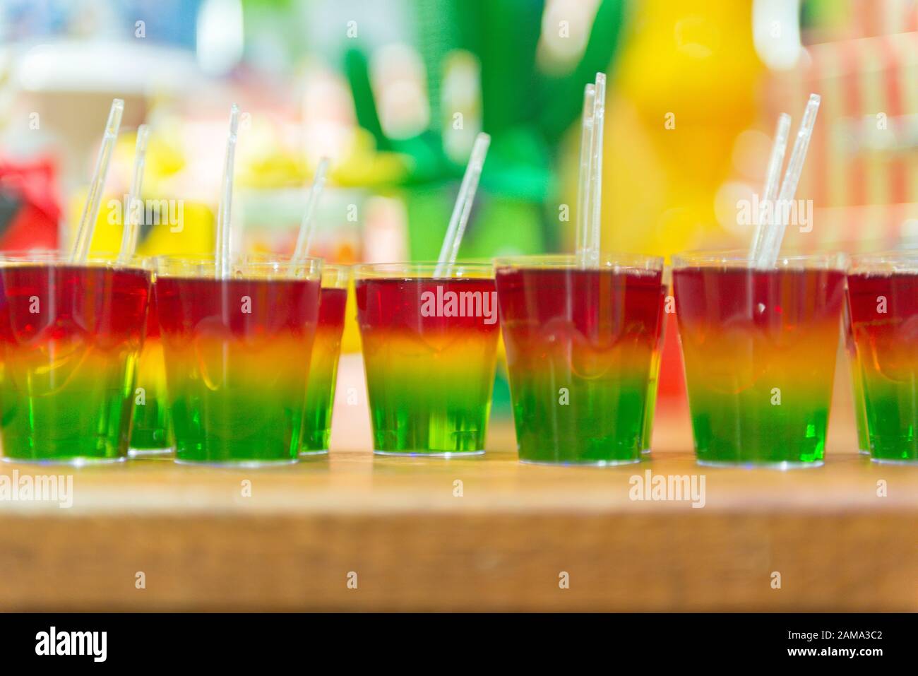 Glass with colorful striped jelly above wooden table. Rainbow jelly for ...