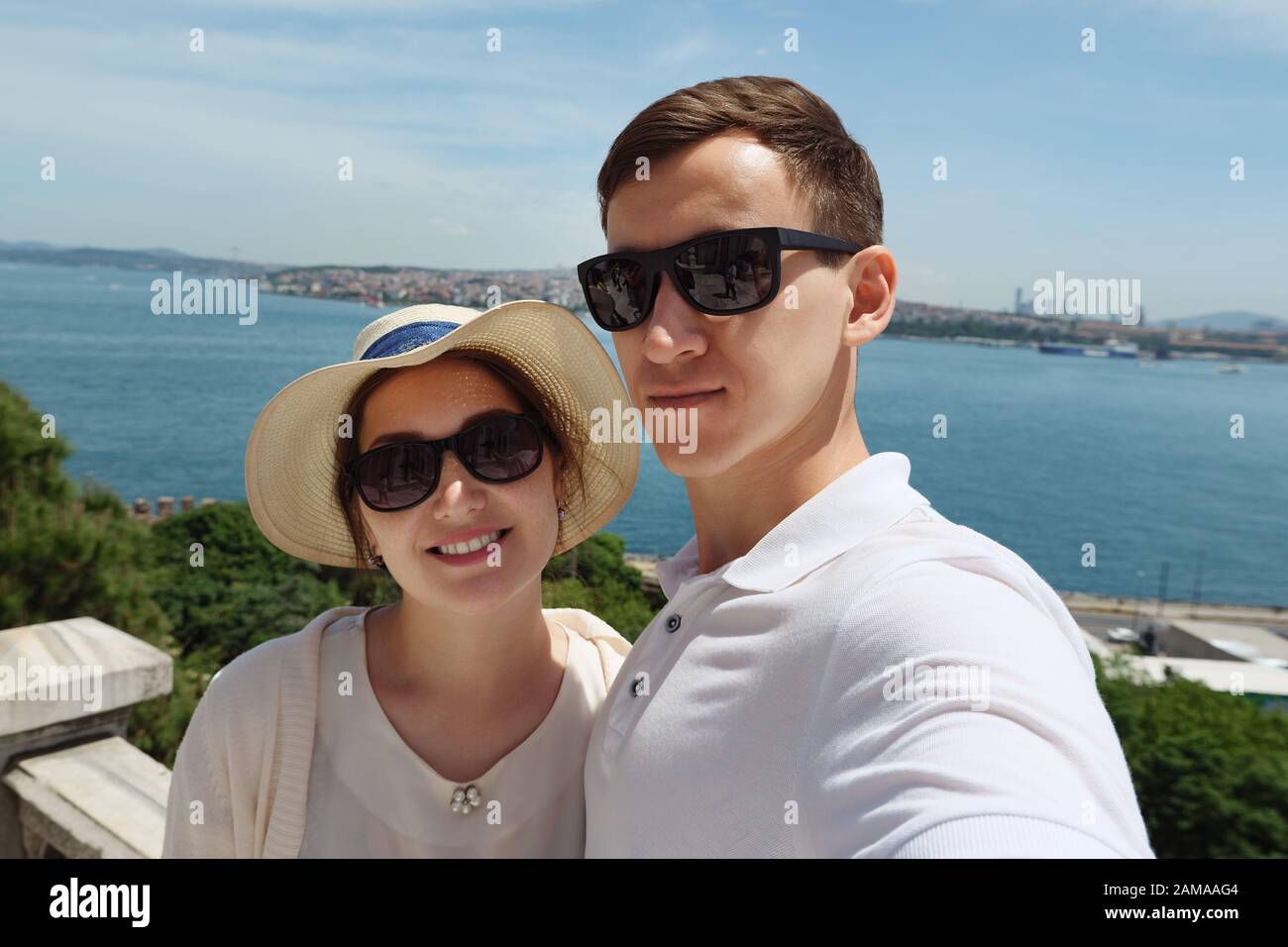happy couple in sunglasses stands on hill and poses kissing against ...