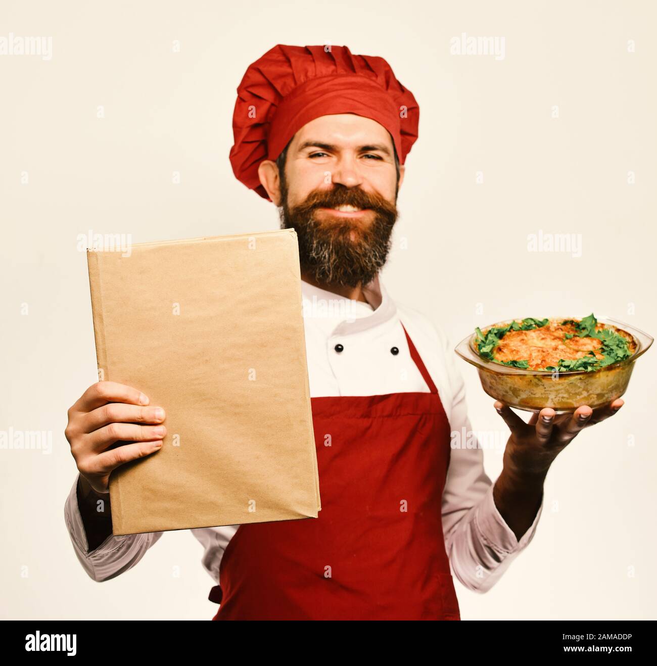 Cook with proud smile in burgundy uniform holds baked dish and menu ...