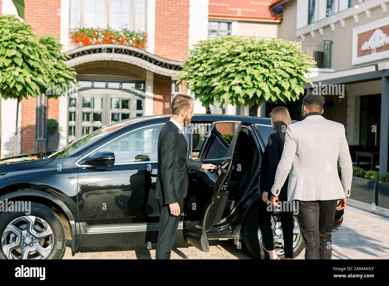 Chauffeur man opening car door for business couple, Caucasian woman and ...