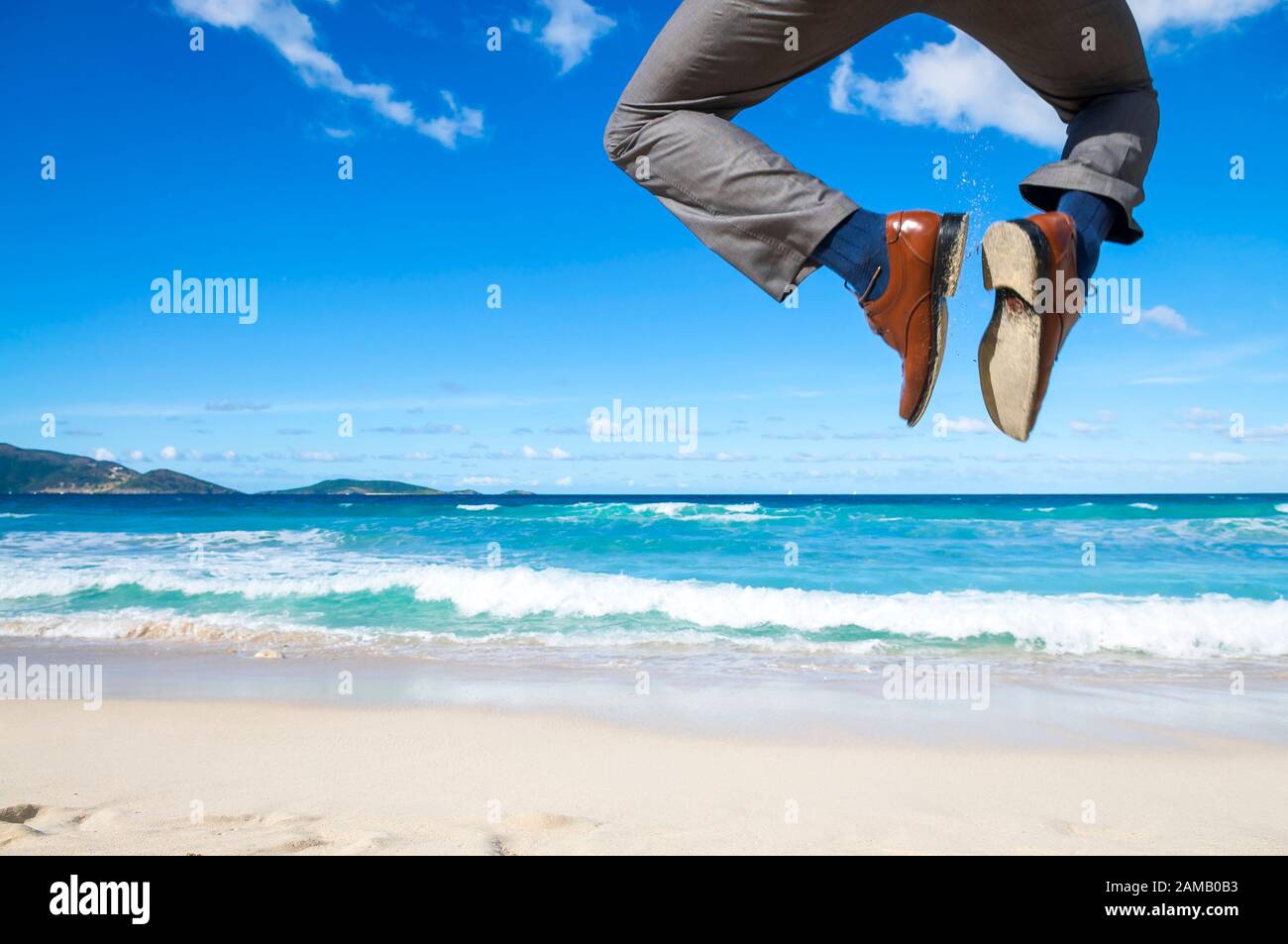 Businessman jumping into the air above a tropical beach clicking his ...