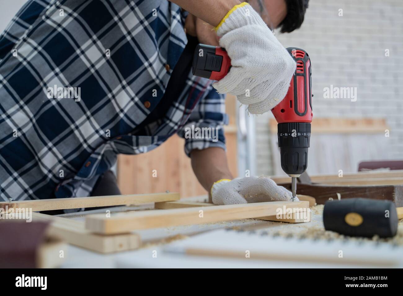 The carpenter is using an electric screwdriver to drill the workpiece ...