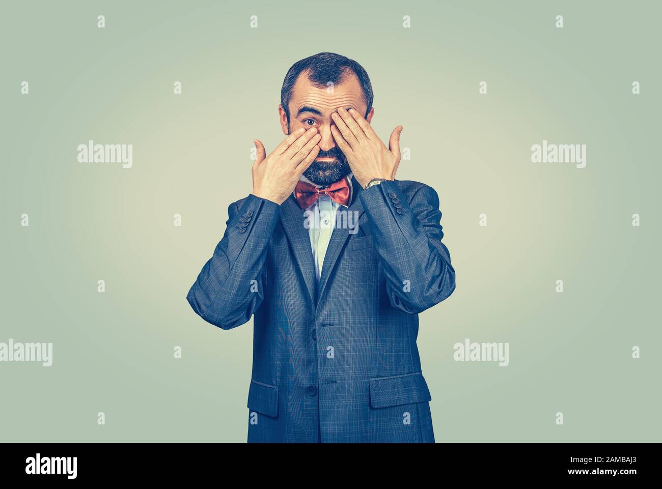 Handsome man with smile covering one eye with hands as he looks sneaky ...