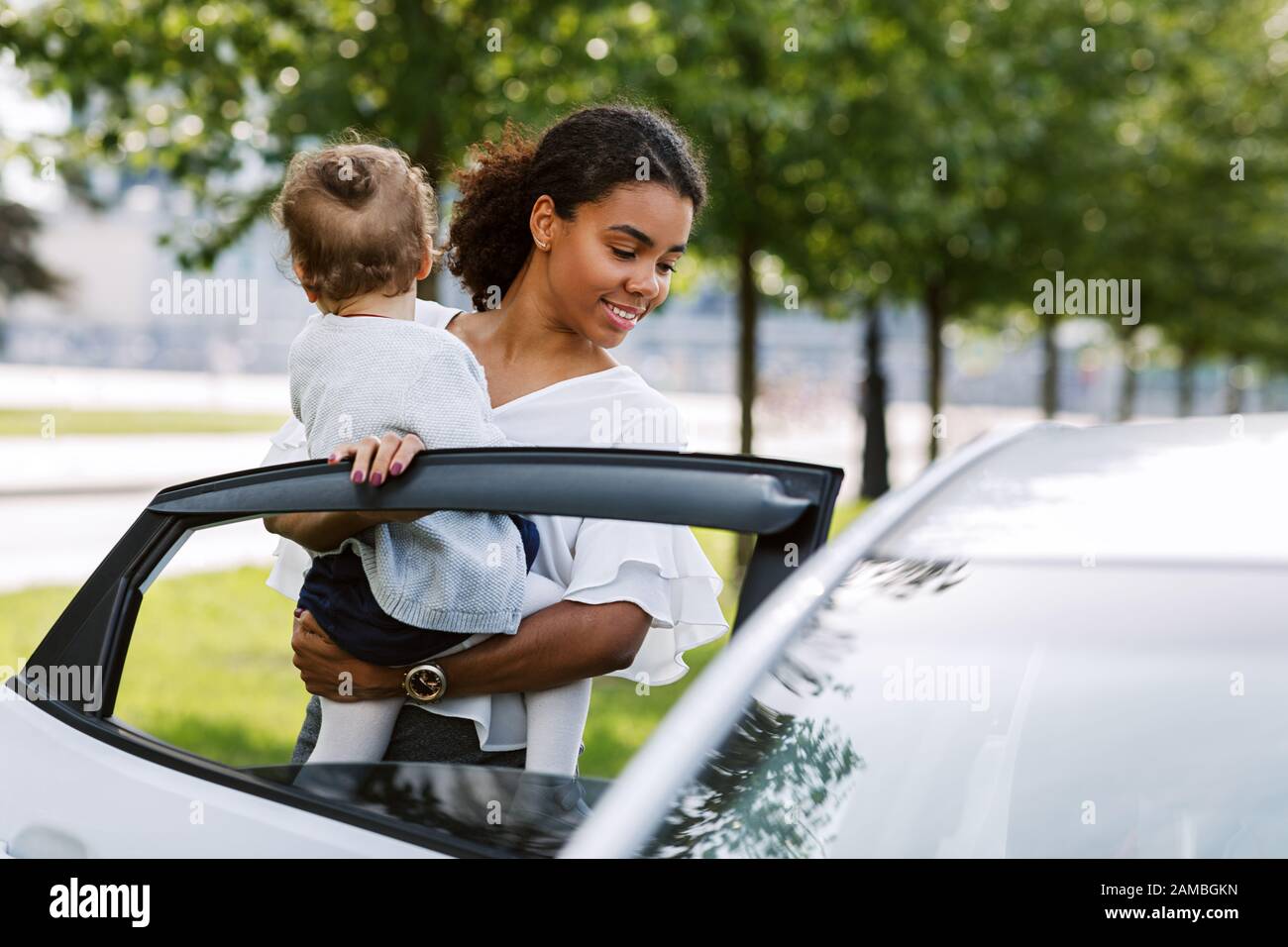 Woman opening a car door and putting her little daughter into it. Young ...