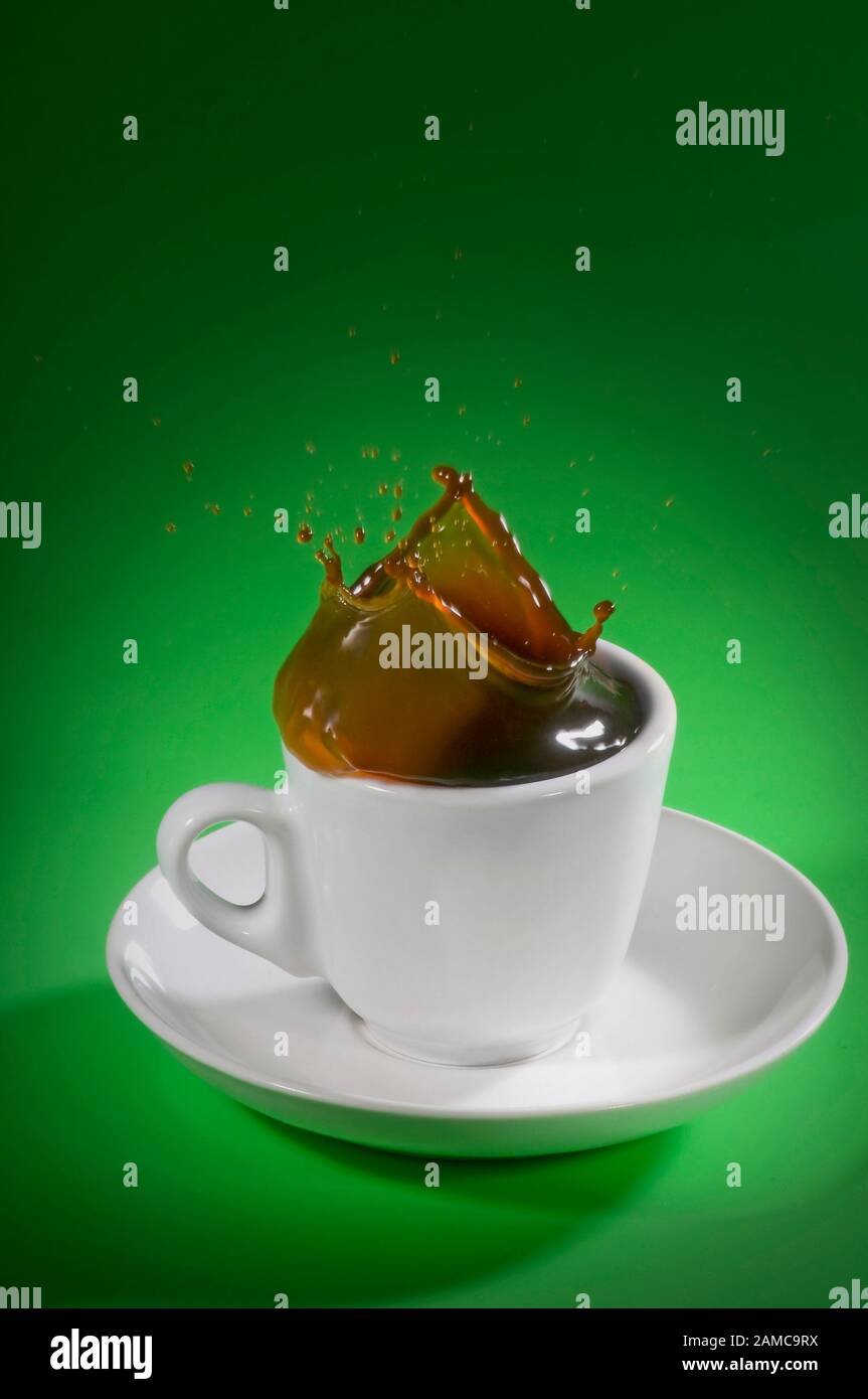 coffee splashing over the edge of a white cup on a green background ...