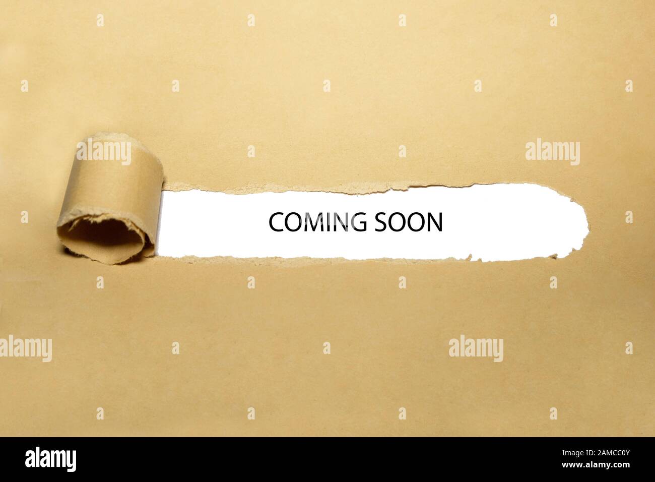 The phrase Coming Soon appearing behind ripped brown paper. Concept ...
