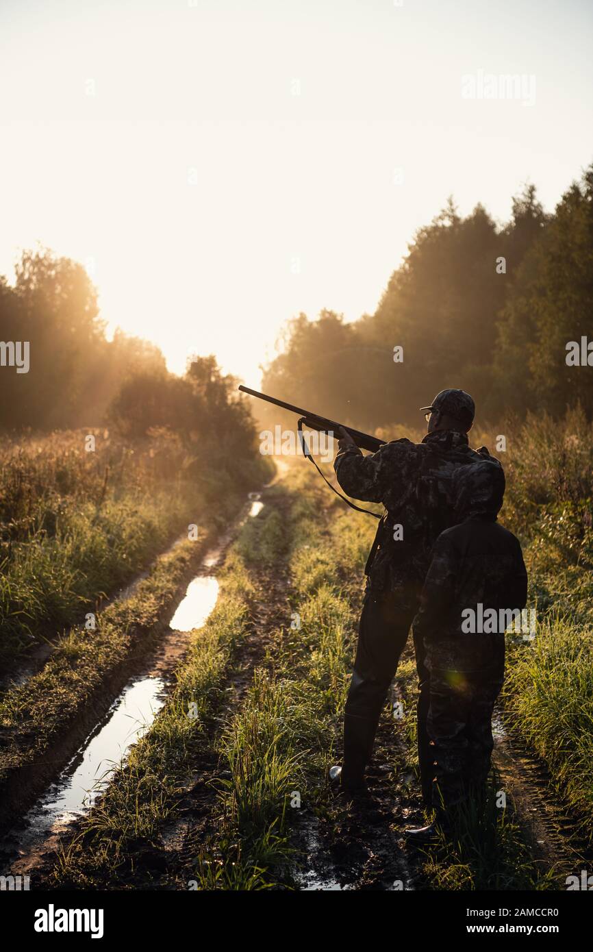 Hunters with hunting equipment going away through rural field towards ...