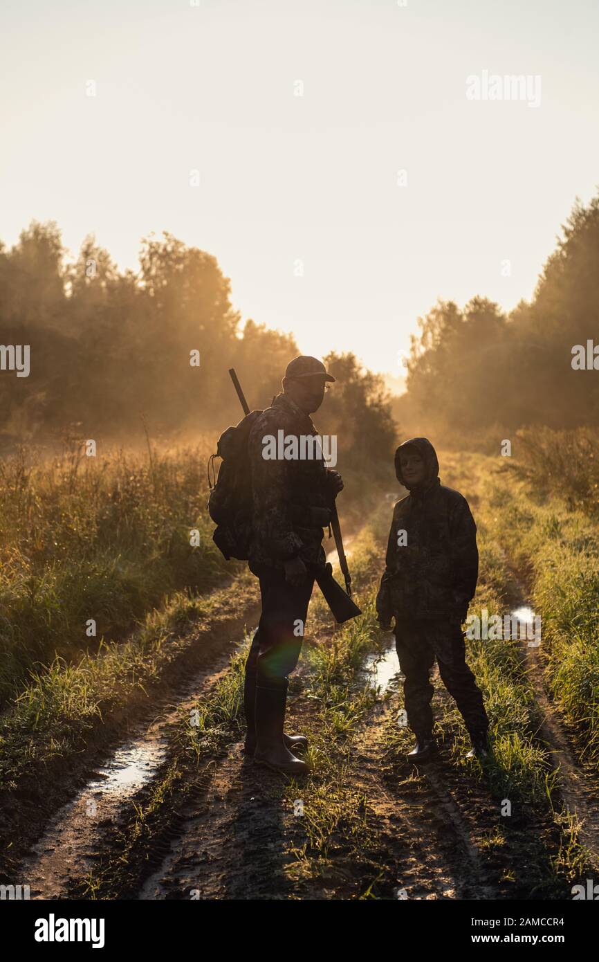 Hunters with hunting equipment going away through rural field towards ...