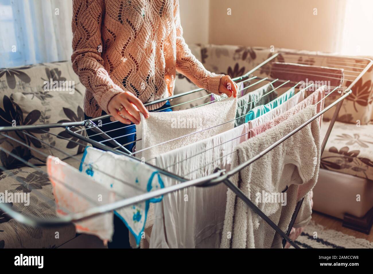 Woman hanging clean clothes on dryer after washing at home ...