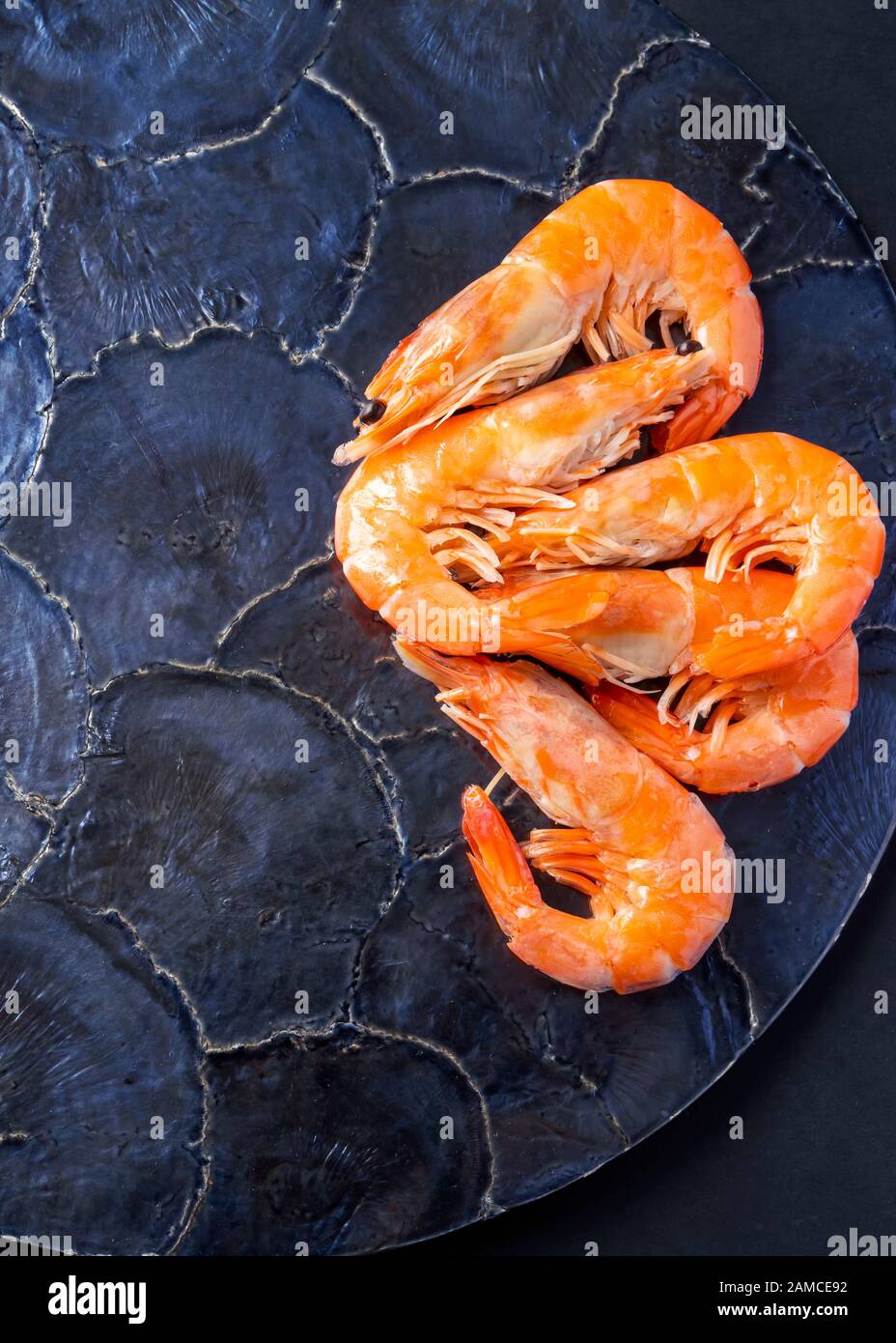 vertical image of group of cooked king prawns on a blue shell plate ...