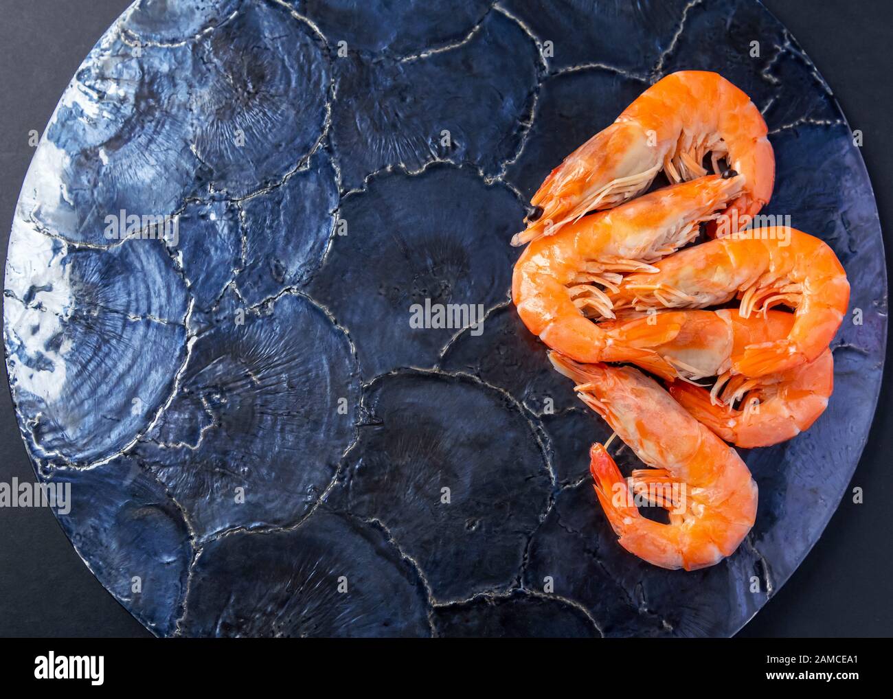 horizontal image of group of cooked king prawns on a blue shell plate ...