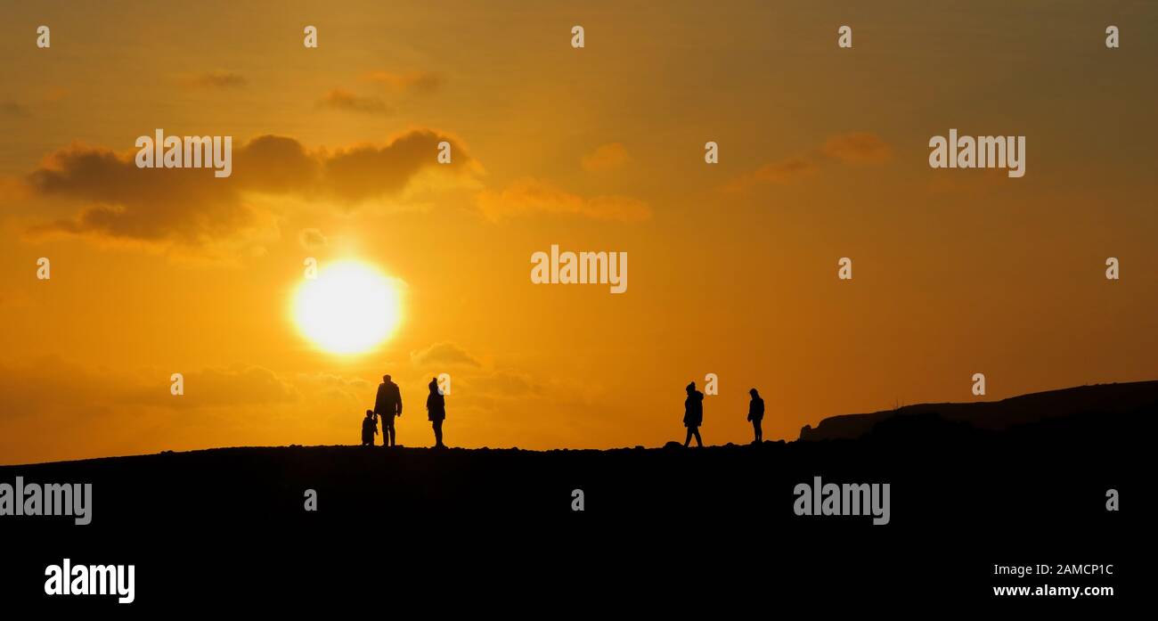 Silhouettes of people walk on horizon at sunset. River Axe near town of ...