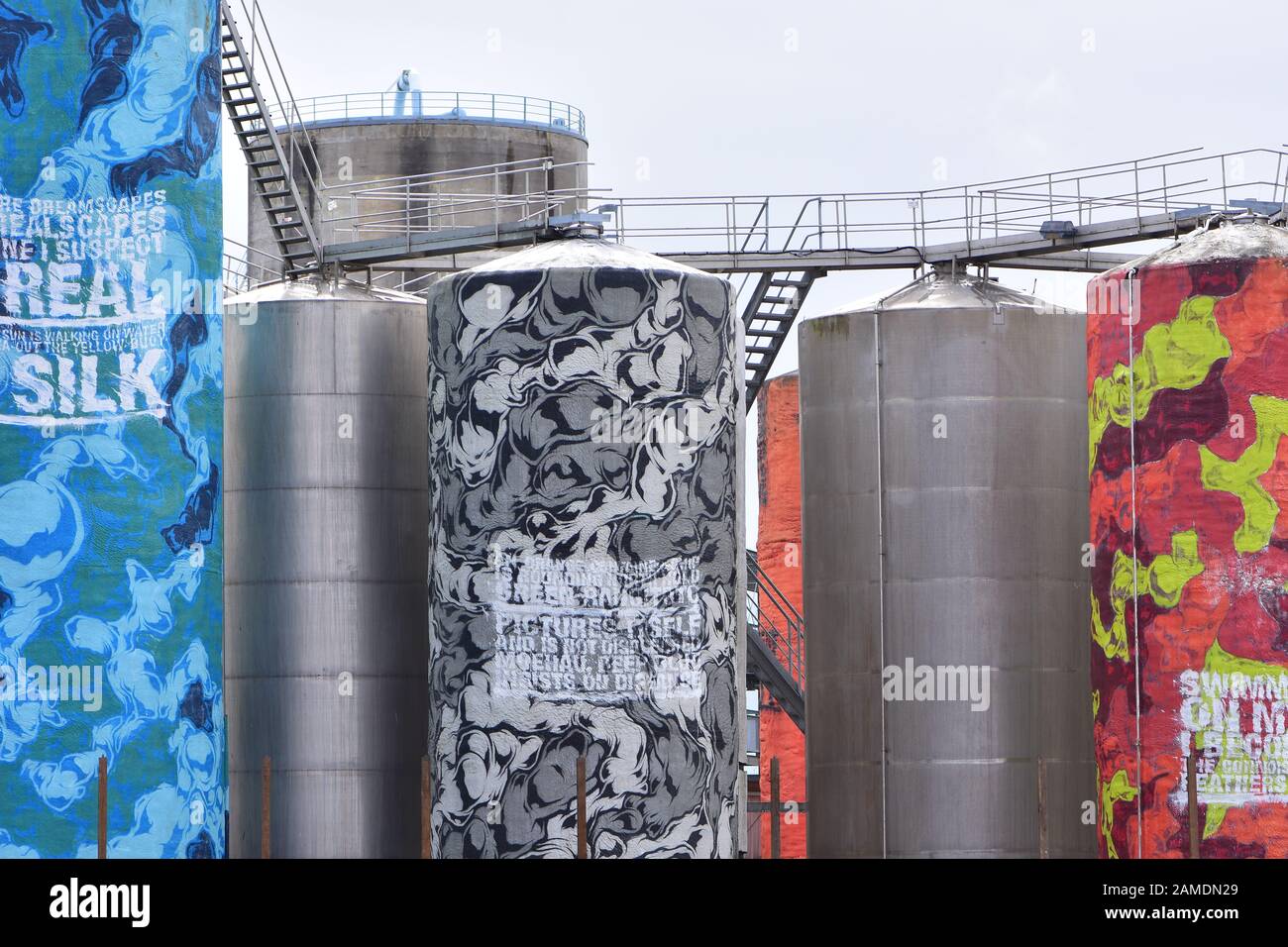 Stainless steel cylindrical industrial silos graffiti painted in bright ...
