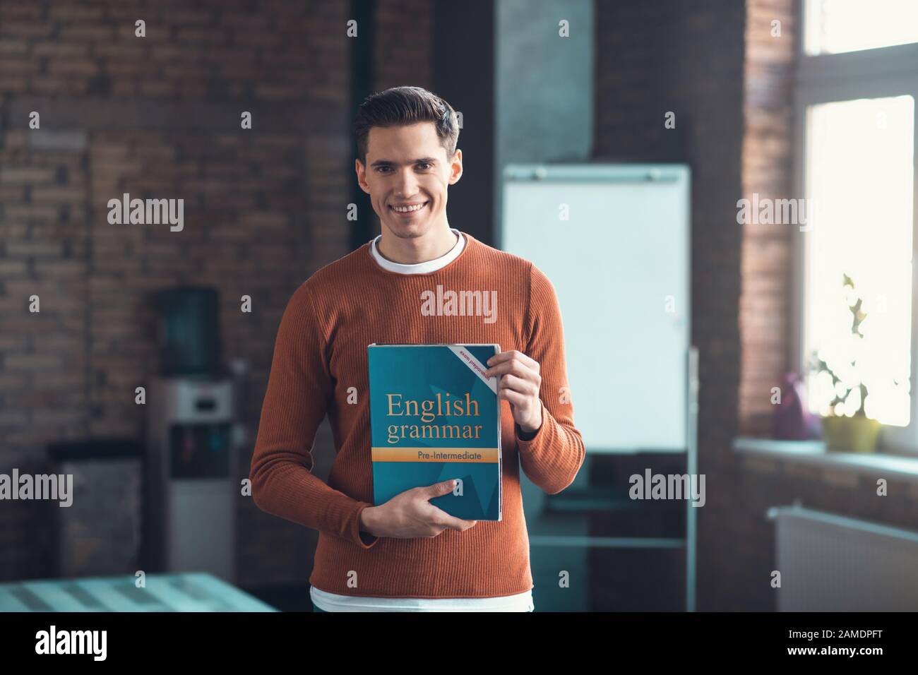 Handsome student smiling while holding English grammar book Stock Photo ...