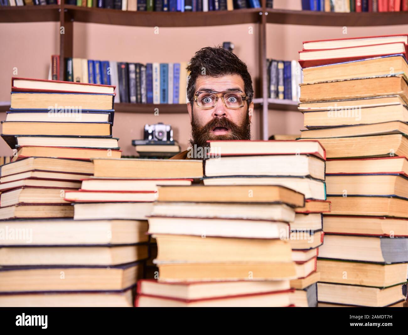 Man, nerd on surprised face between piles of books in library ...