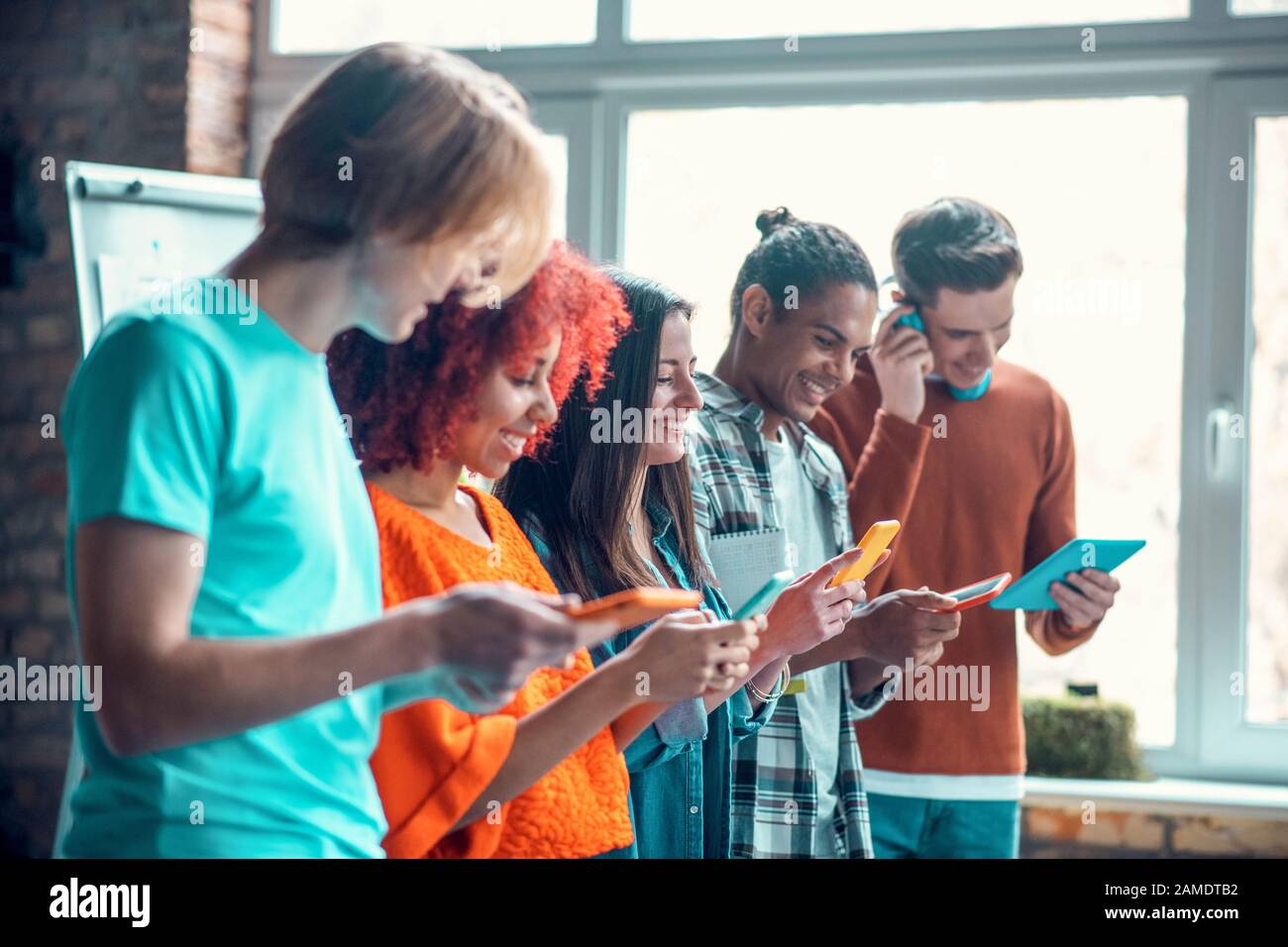 Cheerful students using their gadgets while having little break Stock ...