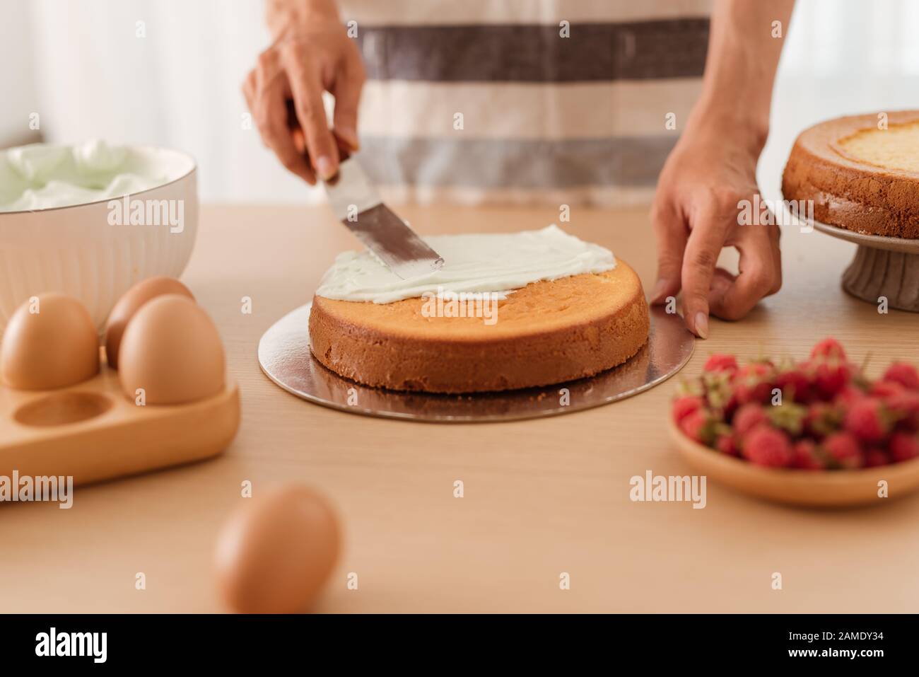 Making of Sponge Cake with Raspberry. Hand putting icing on freshly ...