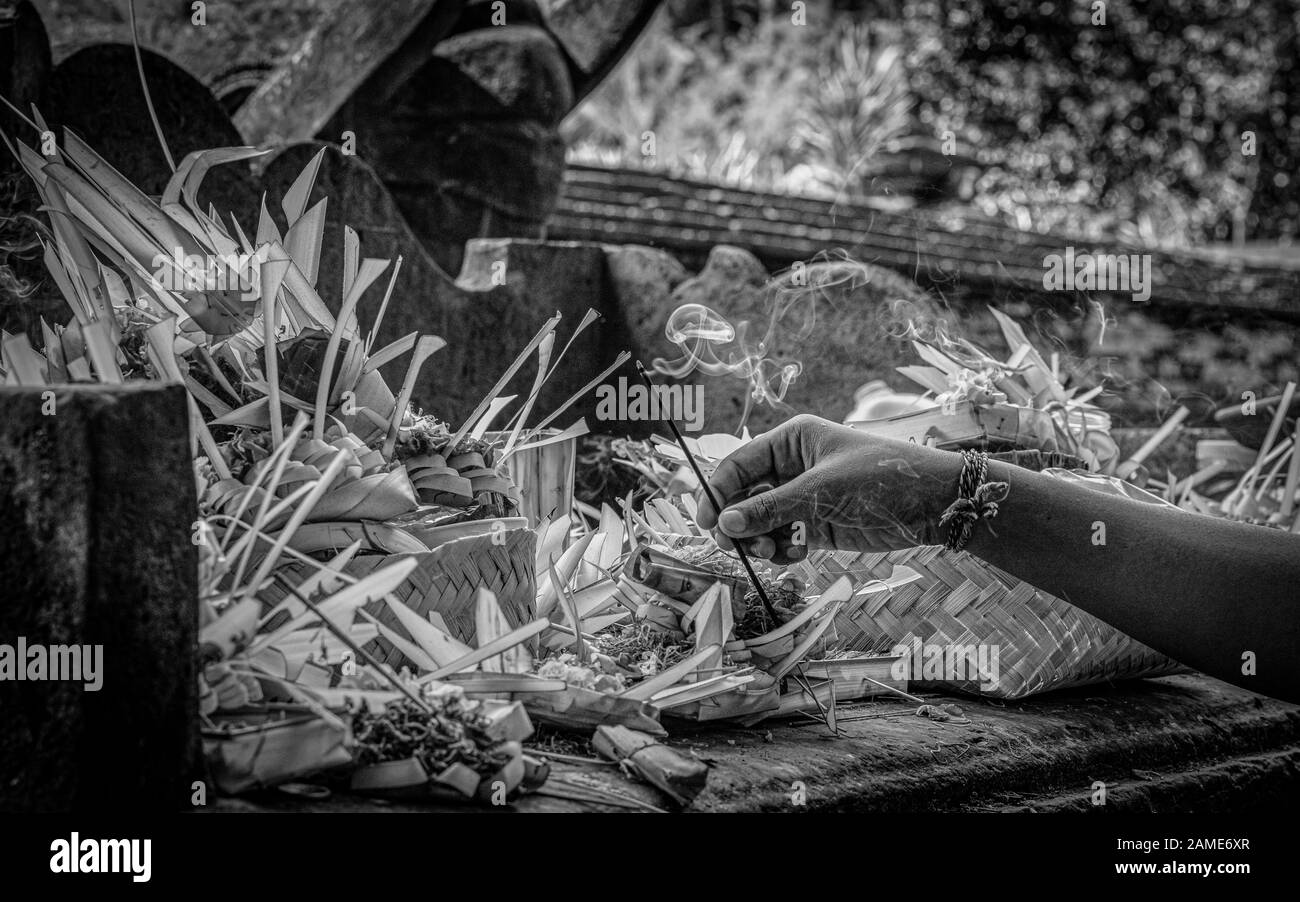 A hand placing burning incense in an offering at a Balinese temple ...