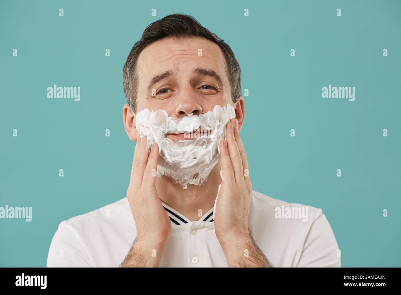 Head and shoulders portrait of smiling adult man shaving and looking at ...