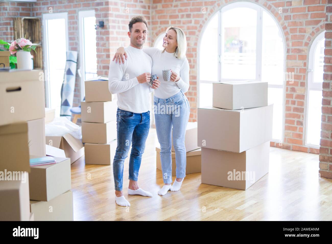 Young Beautiful Couple Standing Drinking Cup Of Coffee At New Home
