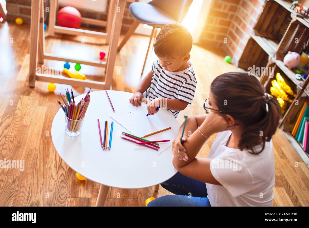 Beautiful teacher and toddler boy drawing draw using colored pencils at ...