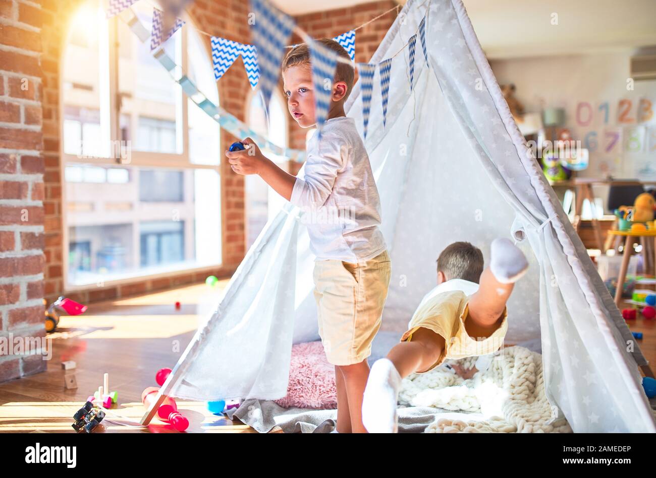 Adorable blonde twins playing inside tipi around lots of toys at ...
