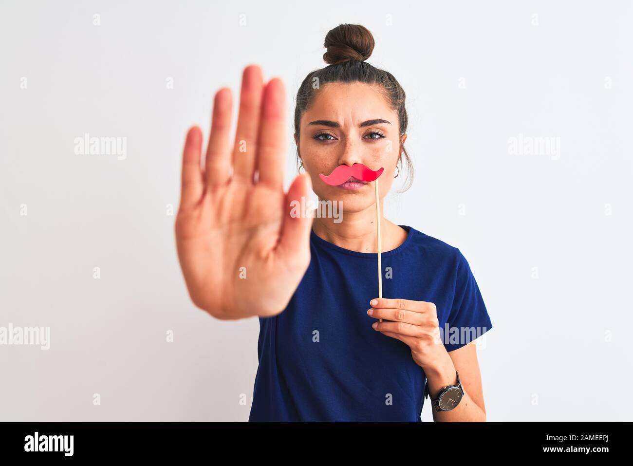 Young beautiful woman holding fanny party mustache over isolated white ...