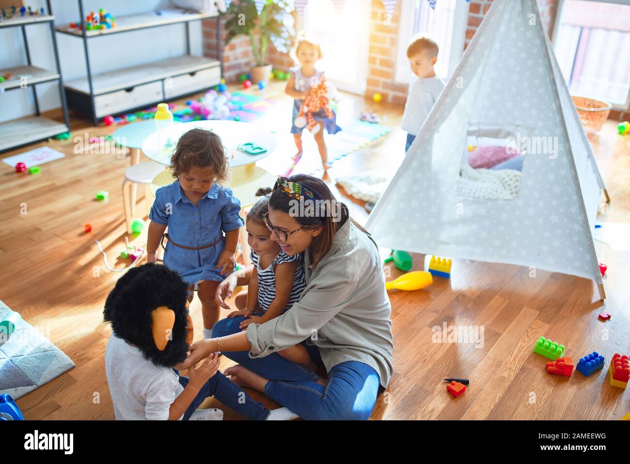 Beautiful teacher and group of toddlers playing around lots of toys at kindergarten Stock Photo ...