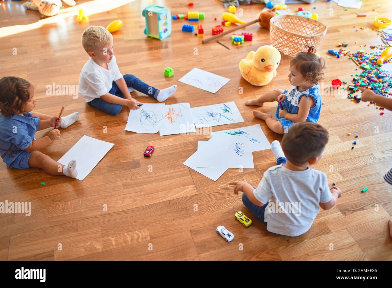 Adorable group of toddlers sitting on the floor drawing using paper and ...