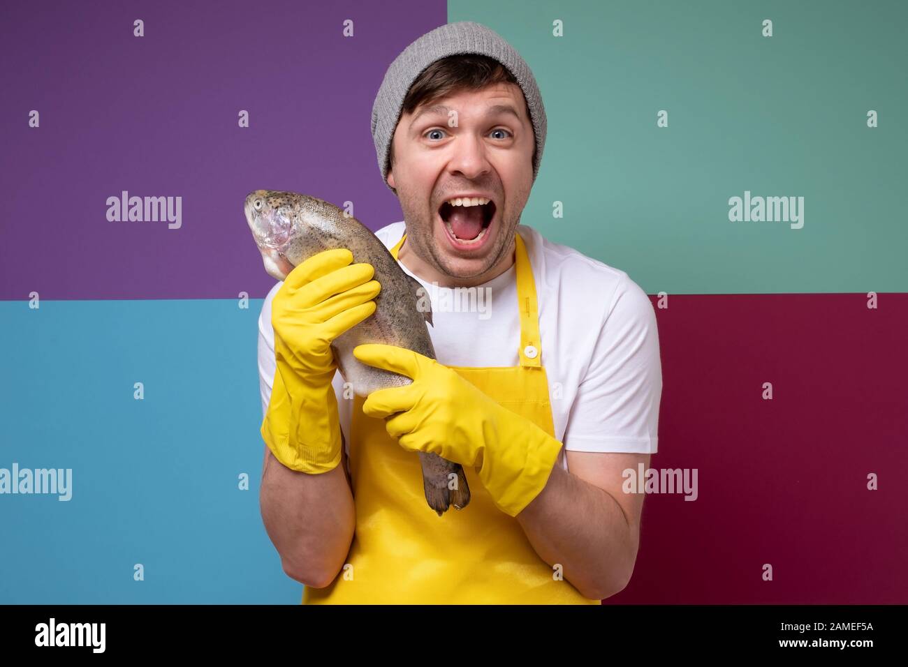 Young male fisher with yellow apron holding a big salmon, trout fish ...
