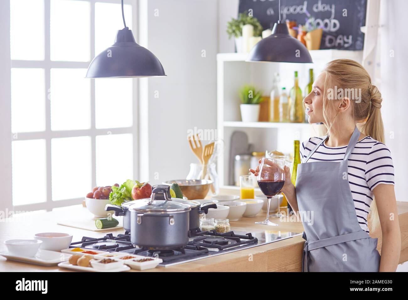 Beautiful woman in kitchen is drinking red wine Stock Photo - Alamy