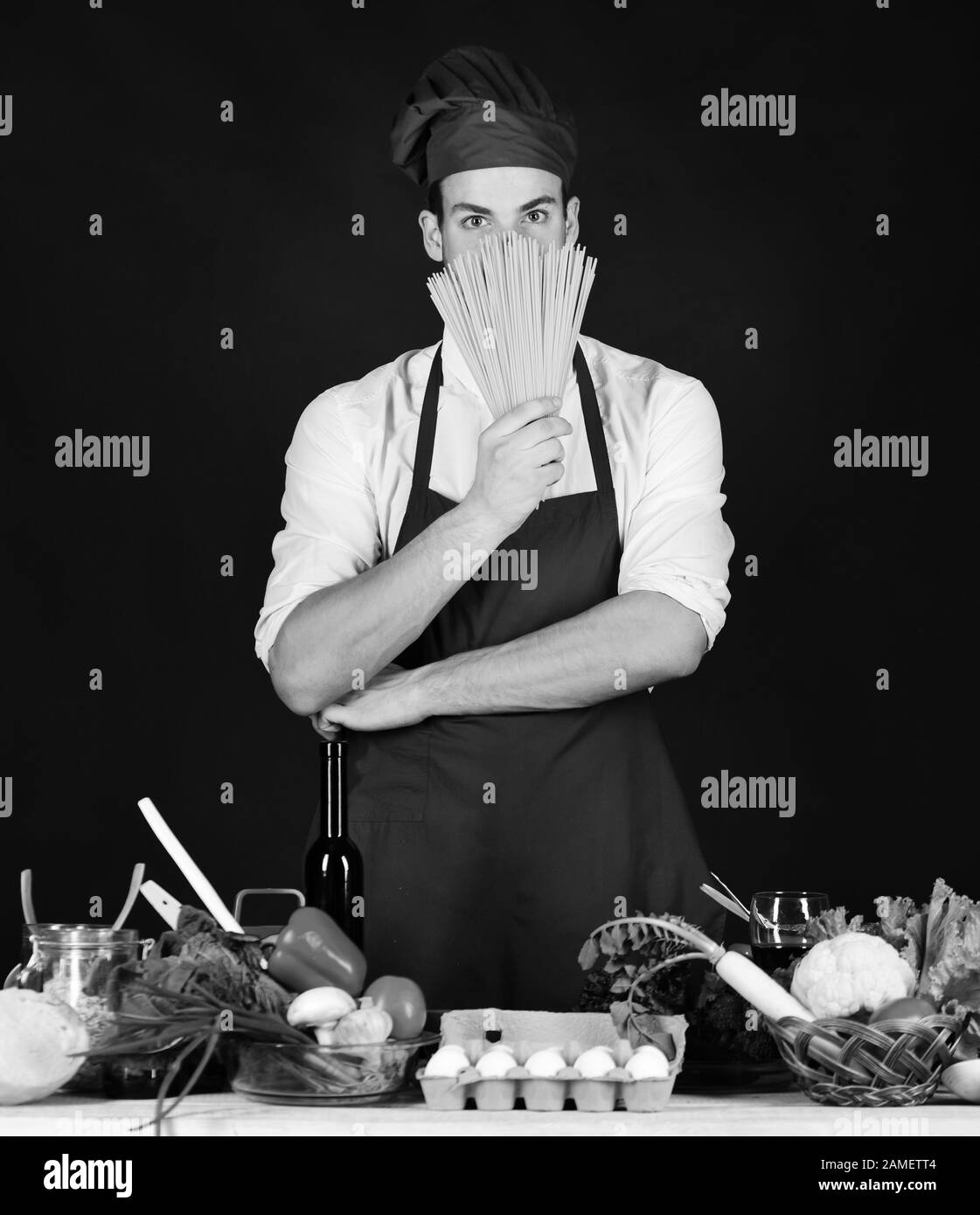 Chef with hidden face holds bunch of spaghetti on black background ...
