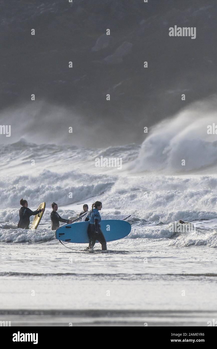 A female surfer carrying her surfboard and walking into a rough sea in ...