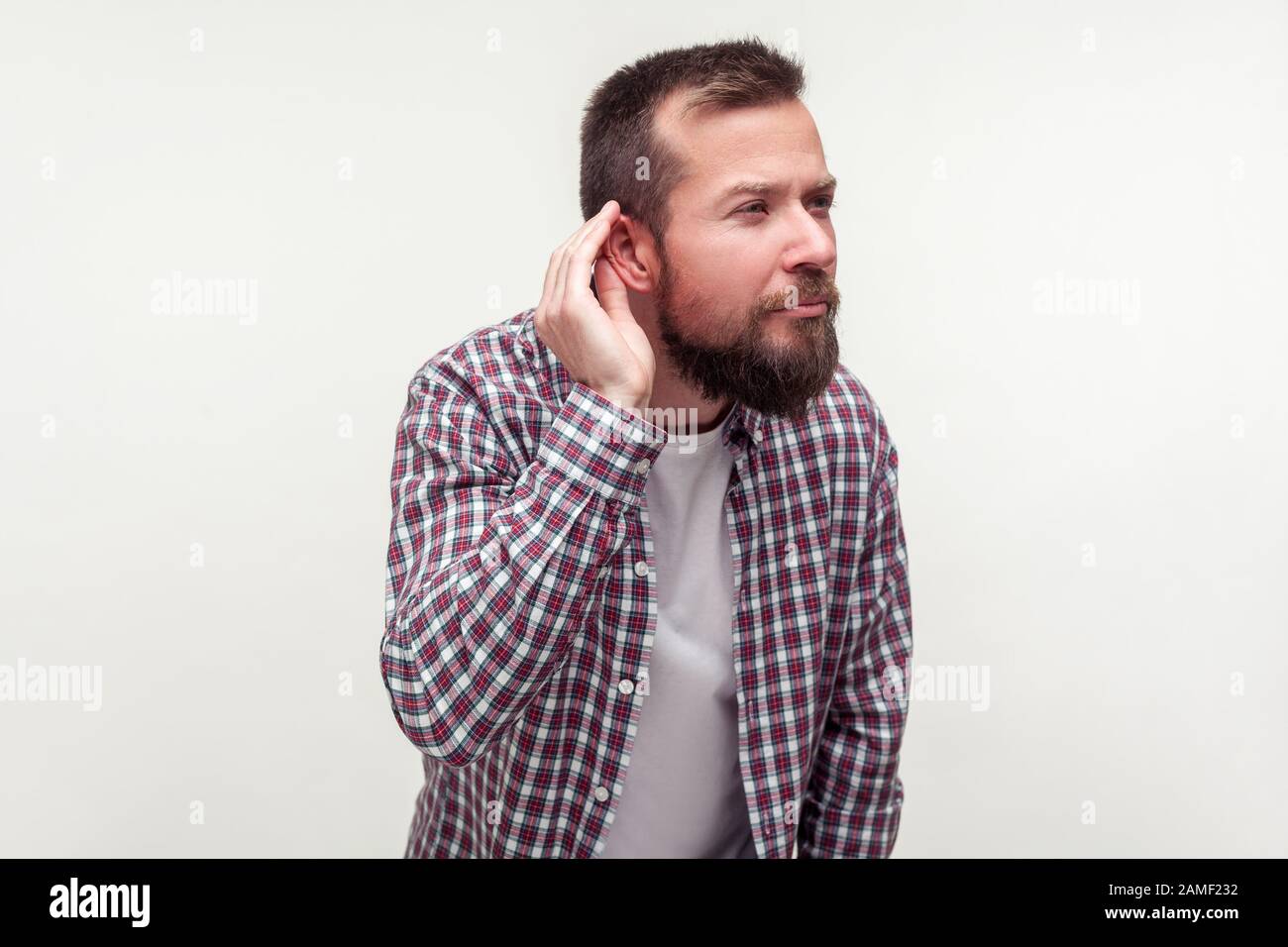 Portrait of deaf bearded man in plaid shirt standing with hand near ear ...