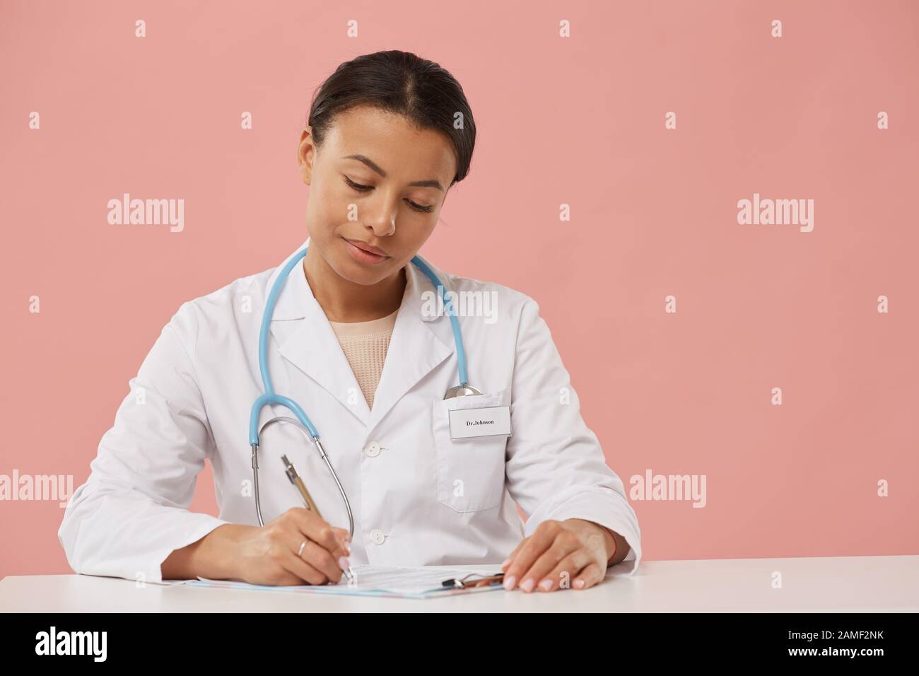 Portrait of beautiful female doctor writing on clipboard while filling ...