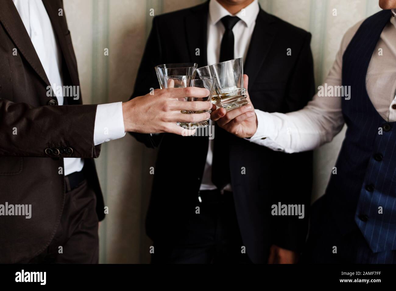 stylish friends businessmen in suits toasting with glasses of whiskey ...