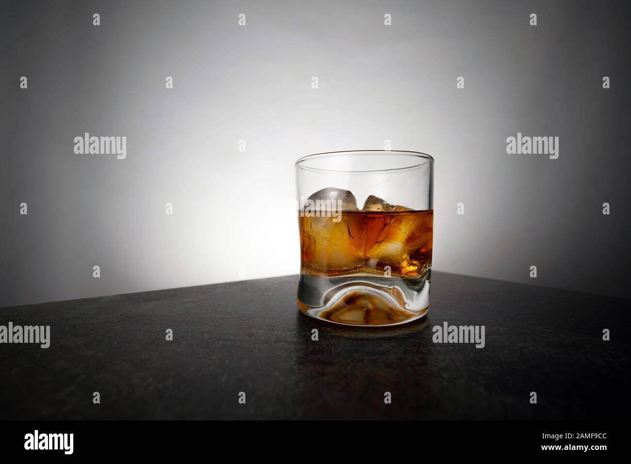 Glass of aged golden whiskey with ice cubes on the table. Amber colored ...