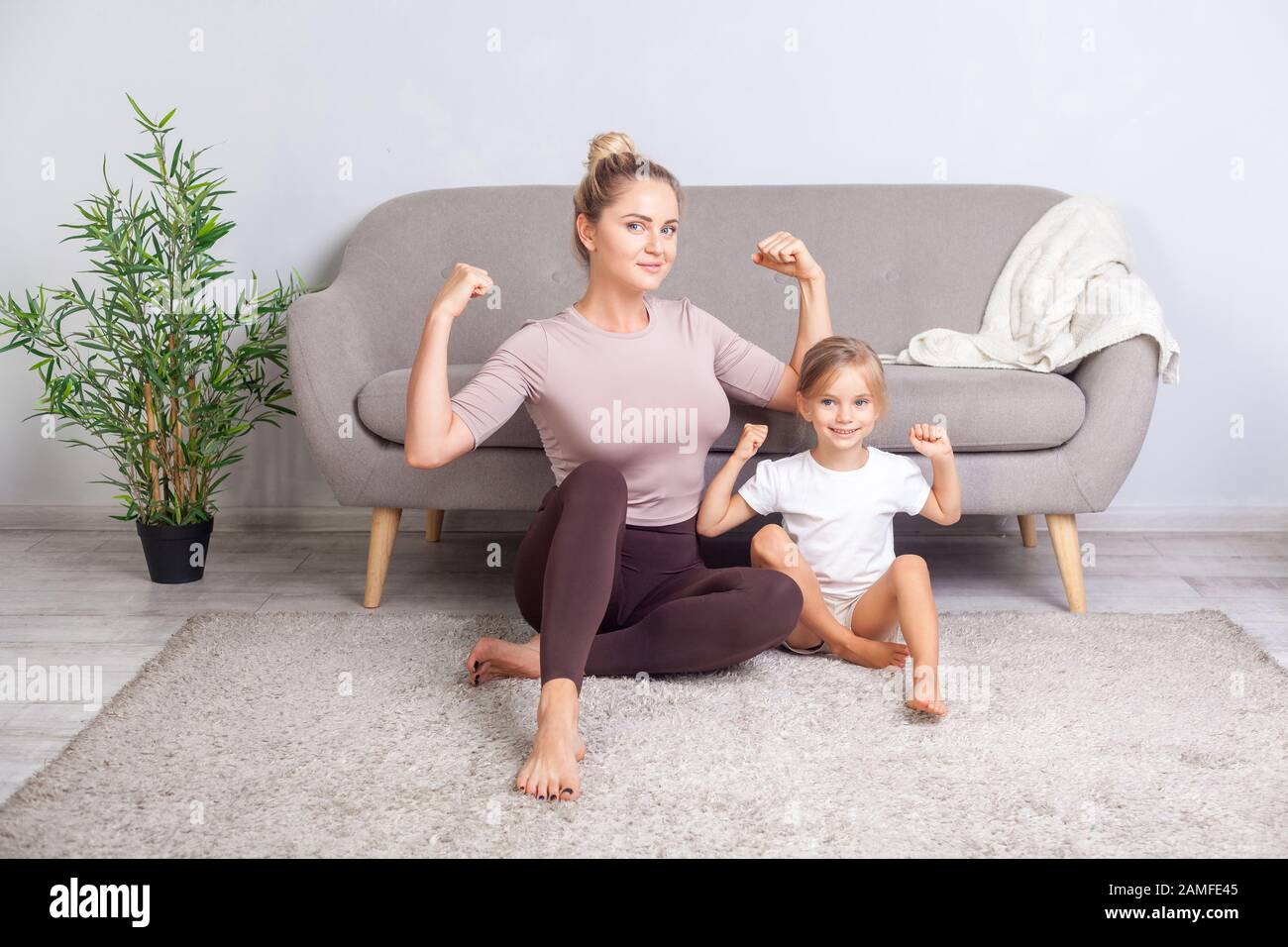 Attractive fit mom and her charming daughter showing biceps, smiling at ...