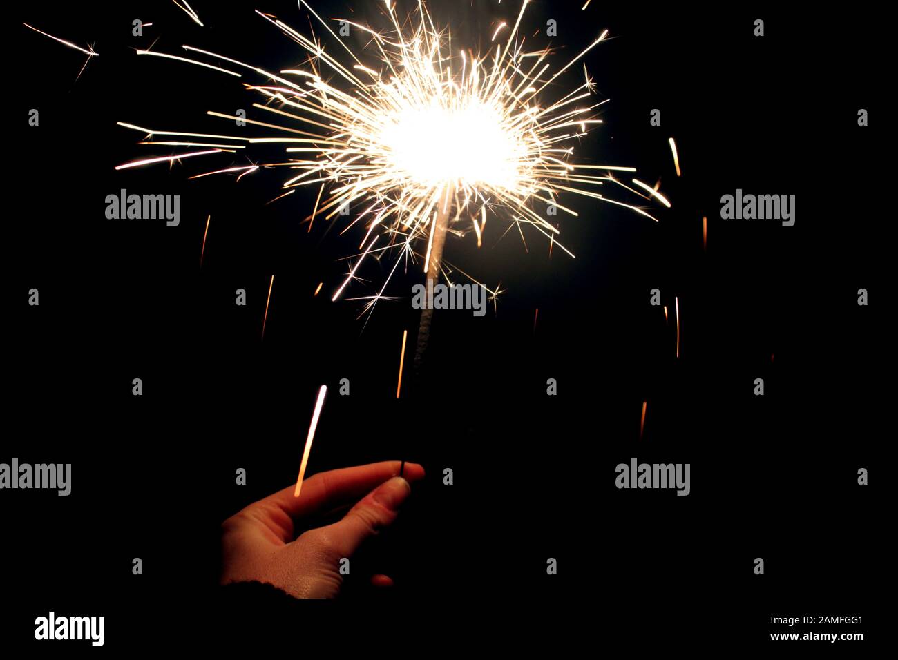 Woman's hand holding burning golden color sparkler in hand in the dark ...