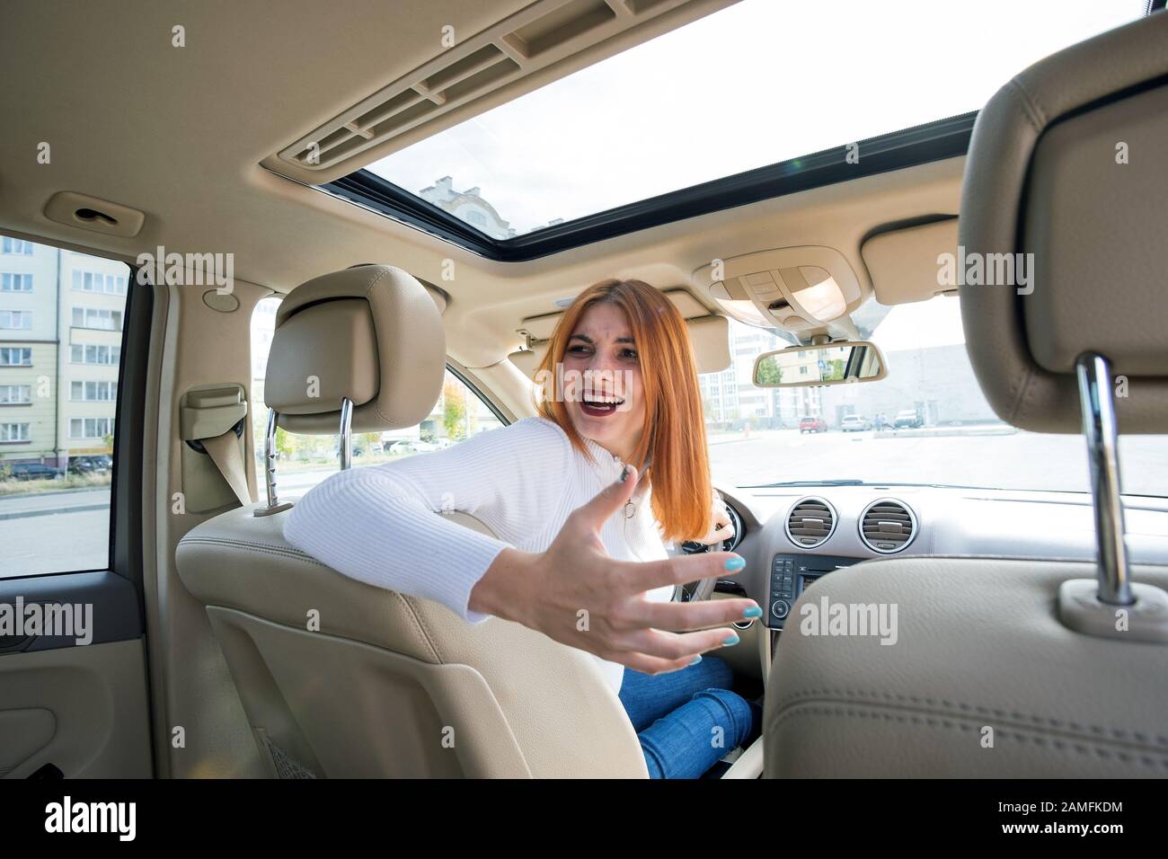 Wide angle view of young redhead woman driver driving a car backwards ...