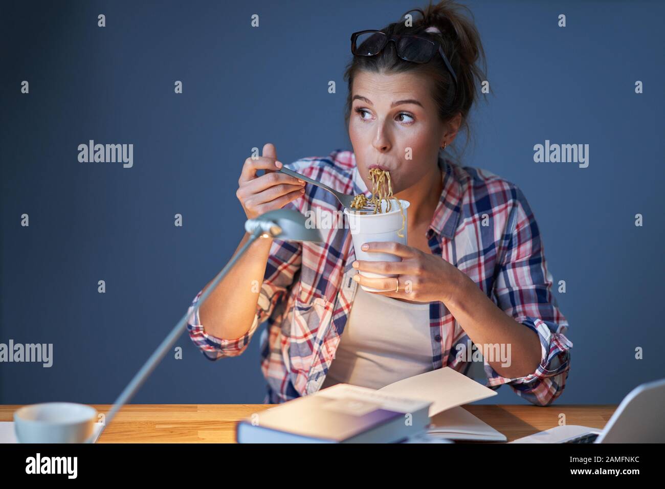 Hungry student eating noodle while learning at home Stock Photo - Alamy