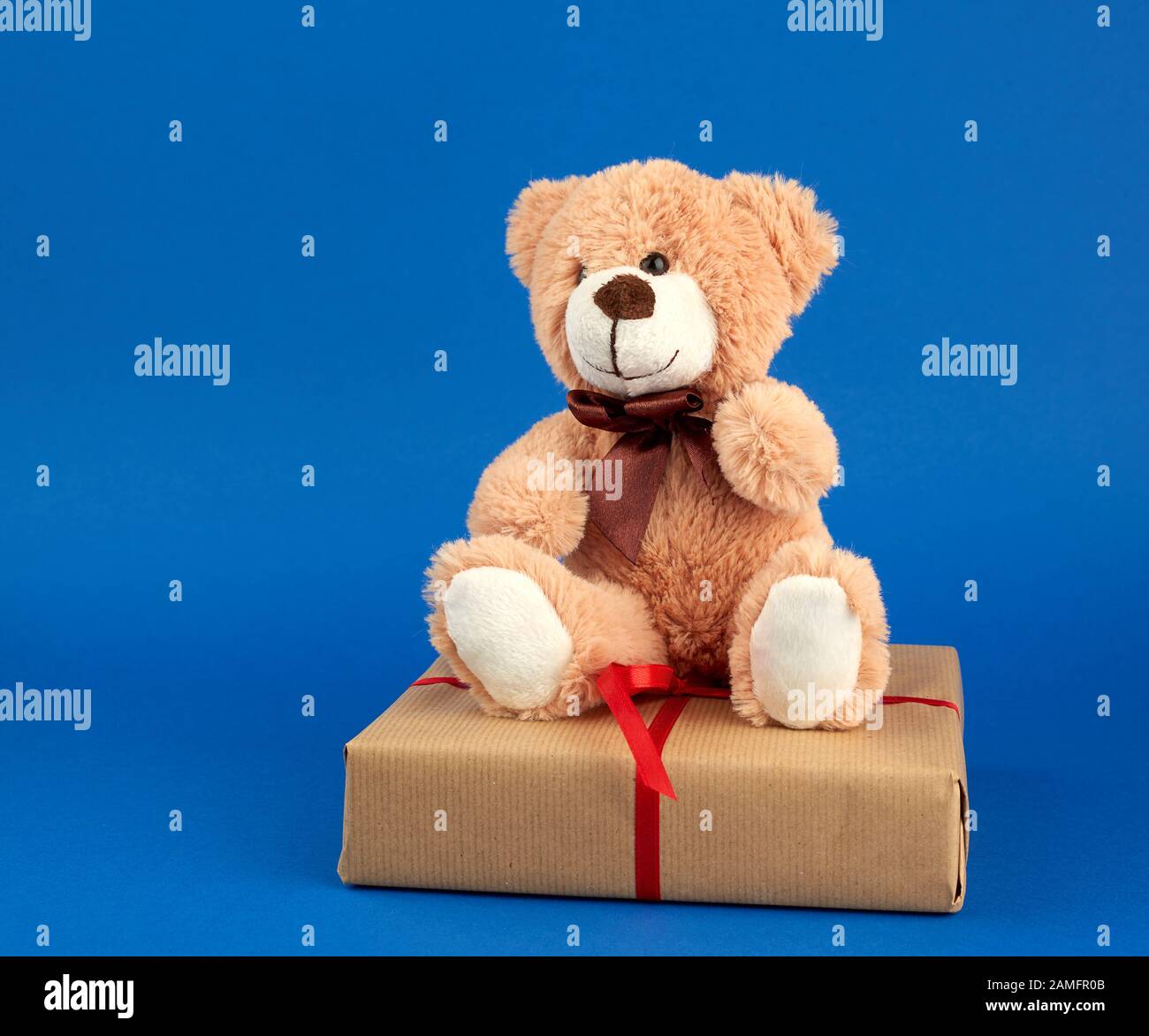 beige teddy bear and a box wrapped in brown kraft paper and tied with a ...