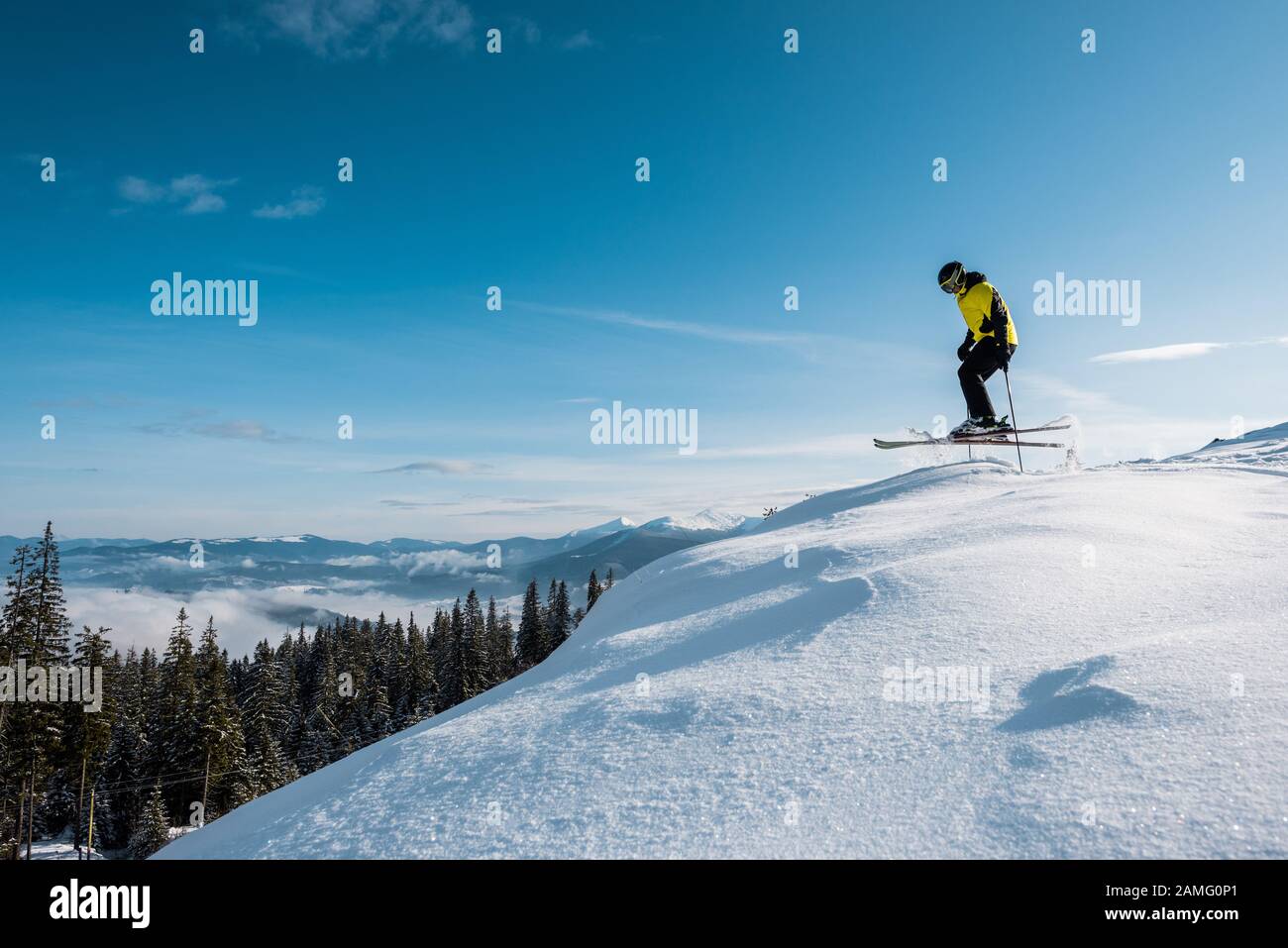 side view of skier holding ski sticks and jumping against blue sky in ...