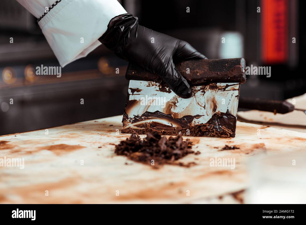cropped view of chocolatier in black latex glove scraping dark ...