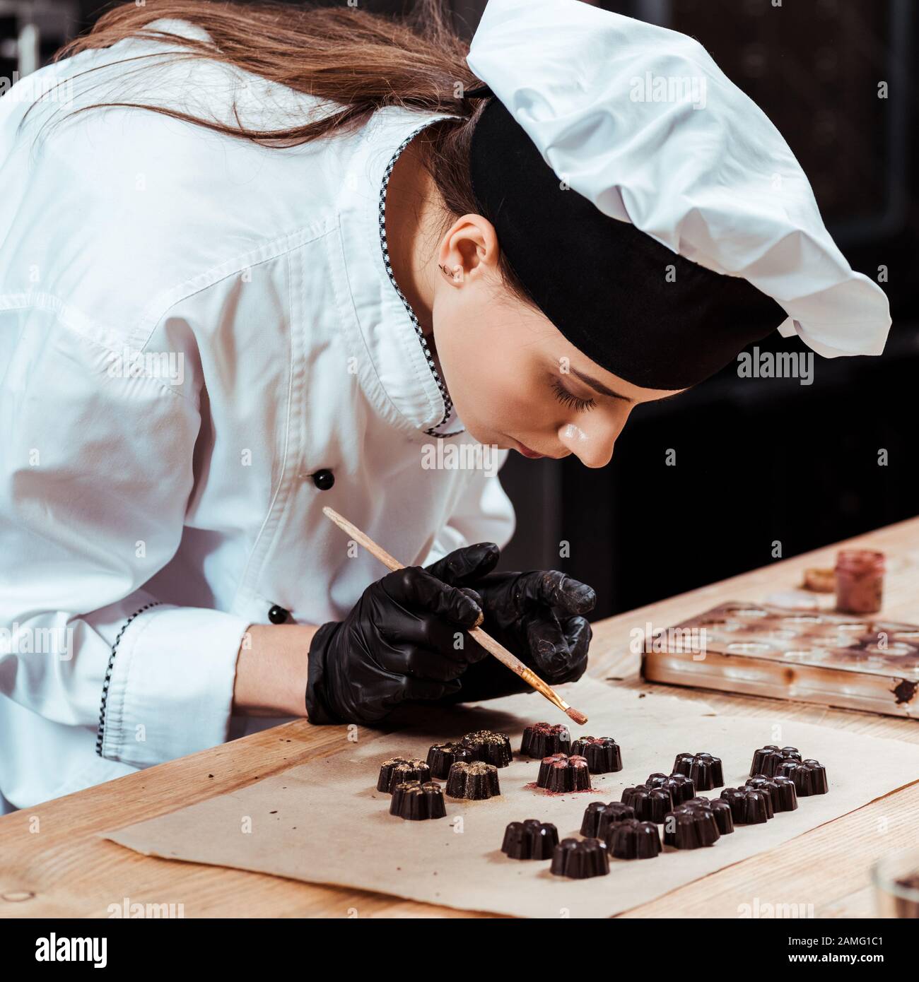 attractive chocolatier holding brush with gold powder near prepared ...