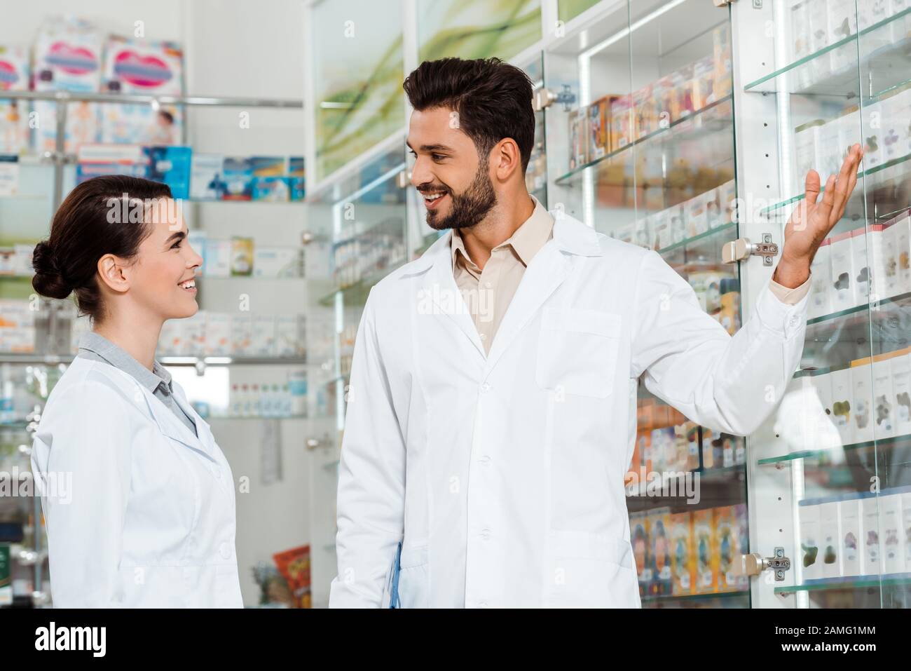 Side view of handsome pharmacist pointing at showcase to colleague in ...