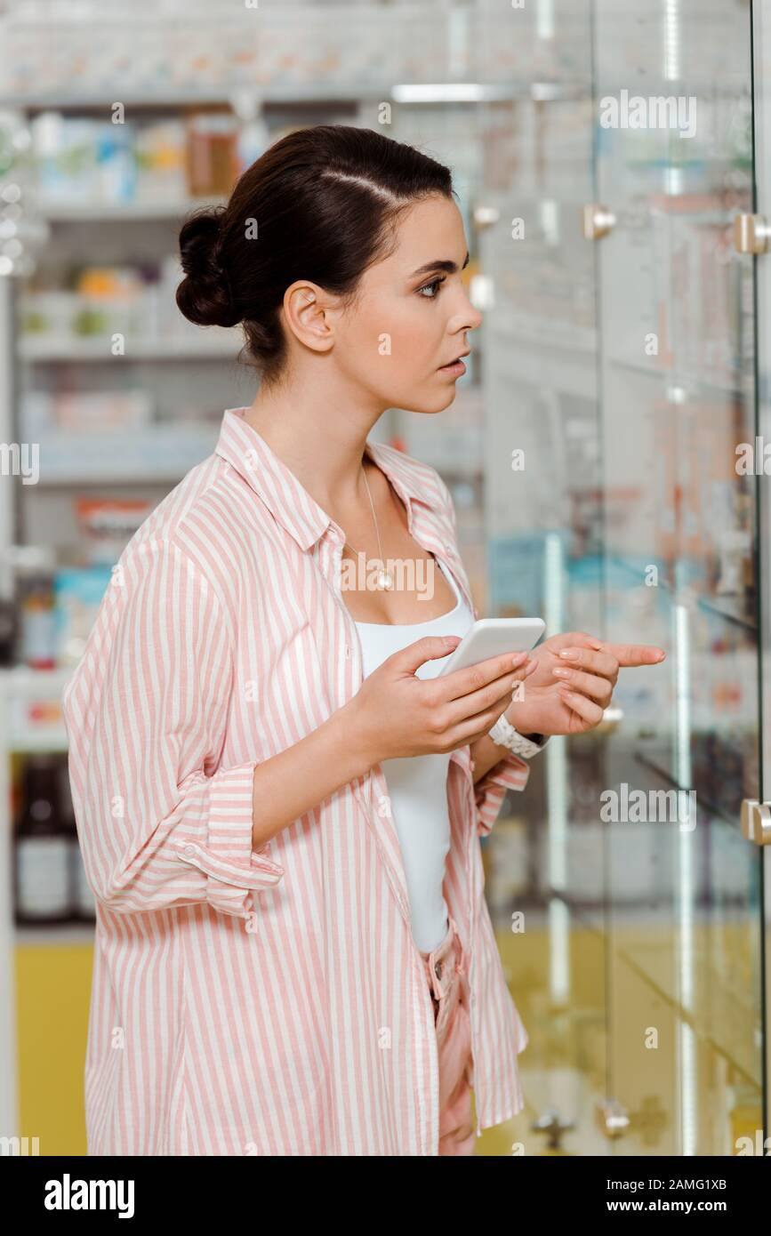 Side view of customer with smartphone looking at showcase in drugstore ...