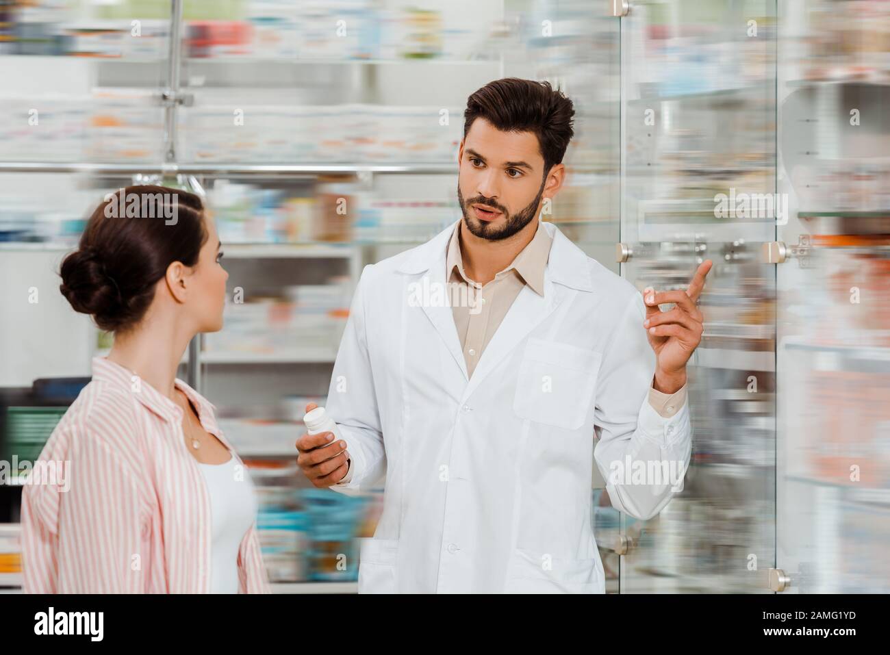 Druggist with pills pointing at medicaments in showcase to customer ...