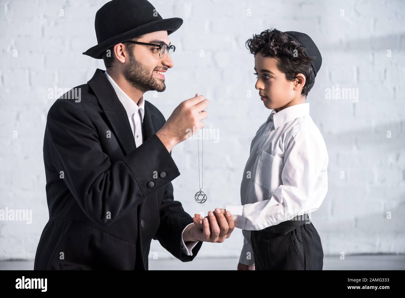 side view of smiling jewish father giving star of david necklace to son ...
