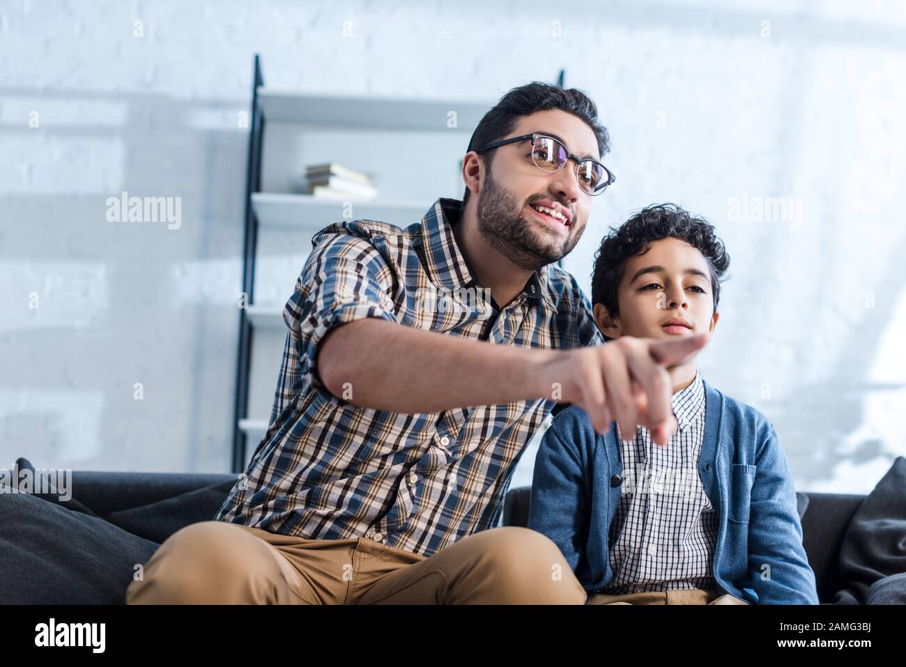 smiling jewish father pointing with finger and watching tv with son ...